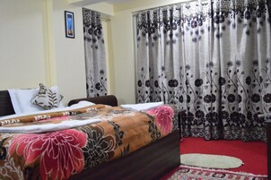 Quarto com cama, mesa de cabeceira, tapete vermelho e cortinas florais.