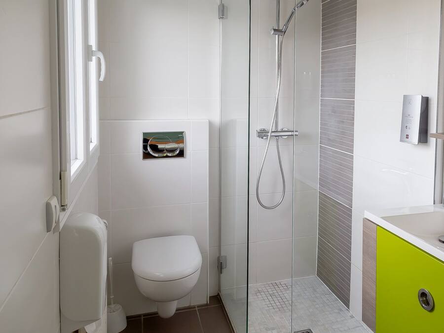 Um banheiro moderno com box de vidro, vaso sanitário branco e toucador verde com pia.