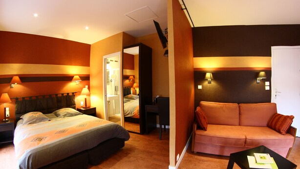 Quarto de hotel com uma cama, um sofá, uma mesinha e um espelho.