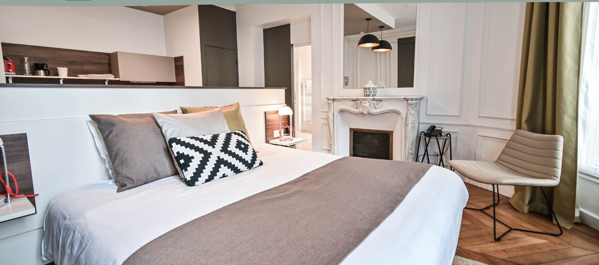 Quarto de hotel com cama, poltrona, lareira e vista para a cidade.