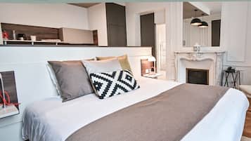 Quarto de hotel com cama, poltrona, lareira e vista para a cidade.