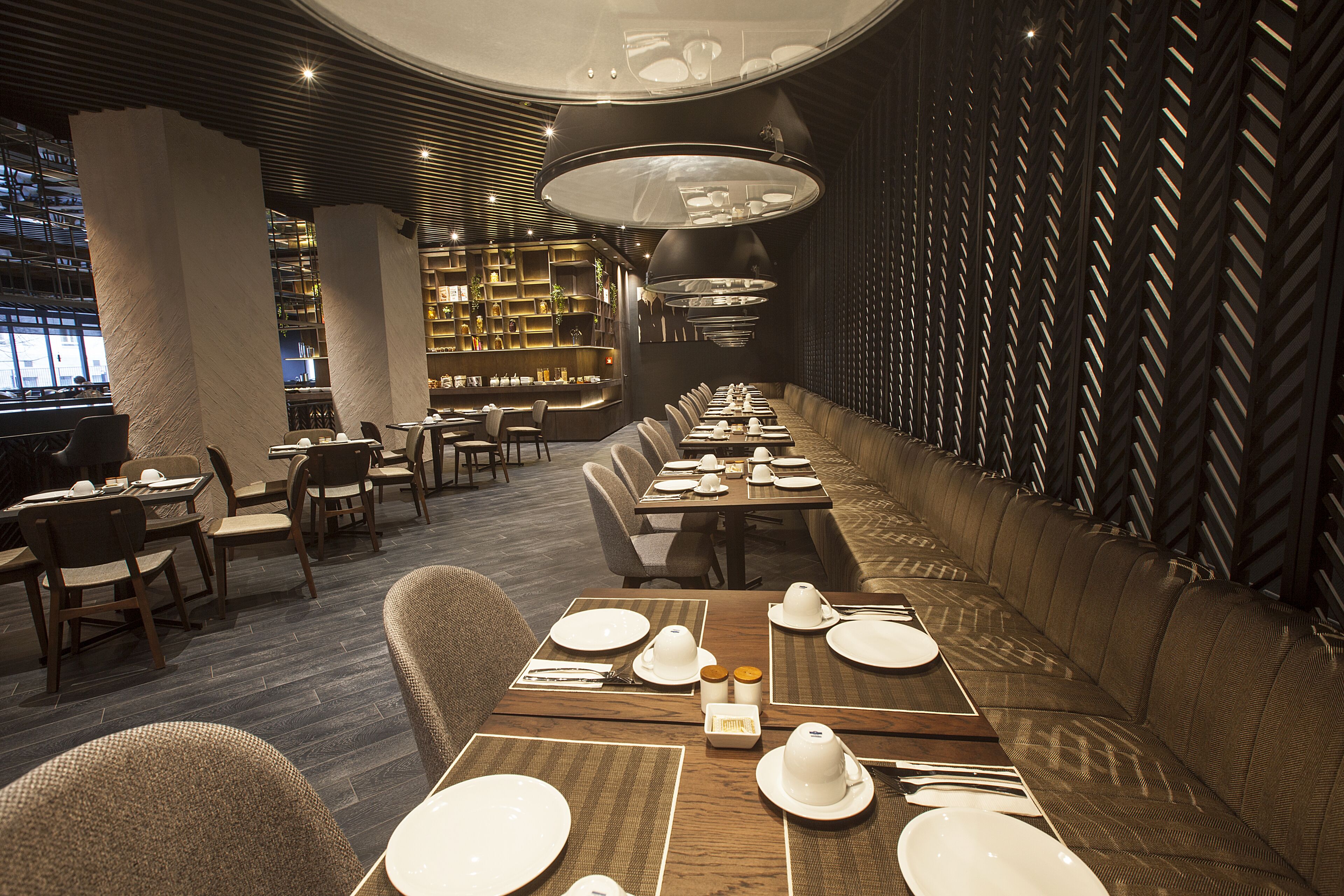 Um restaurante com uma longa mesa de jantar posta para uma refeição, rodeada de cadeiras.