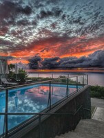 Piscina com barreira de vidro, espreguiçadeiras e guarda-sóis.