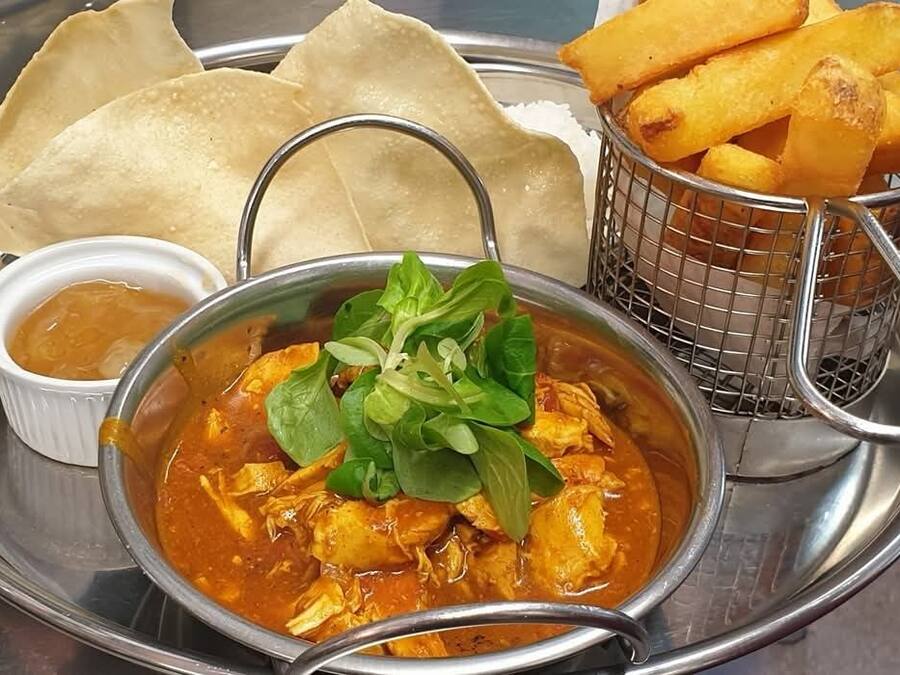 Bandeja de refeição com prato de curry, pão achatado, batatas fritas e um acompanhamento de molho.
