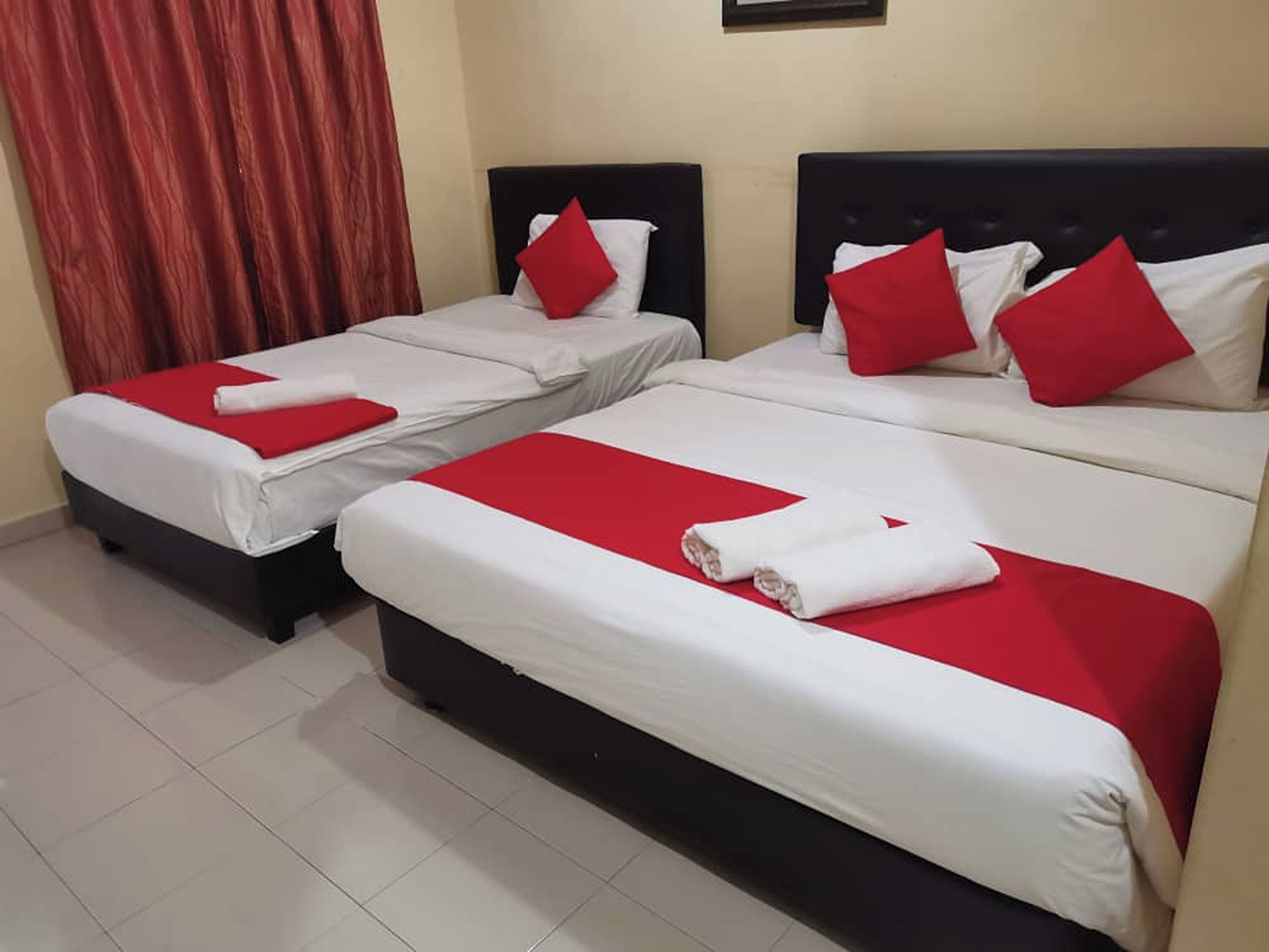 Quarto de hotel com duas camas, cada uma com roupa de cama branca e detalhes vermelhos, e uma cortina vermelha.