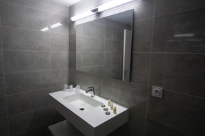 Uma casa de banho moderna com uma pia branca, espelho e azulejos cinzentos.