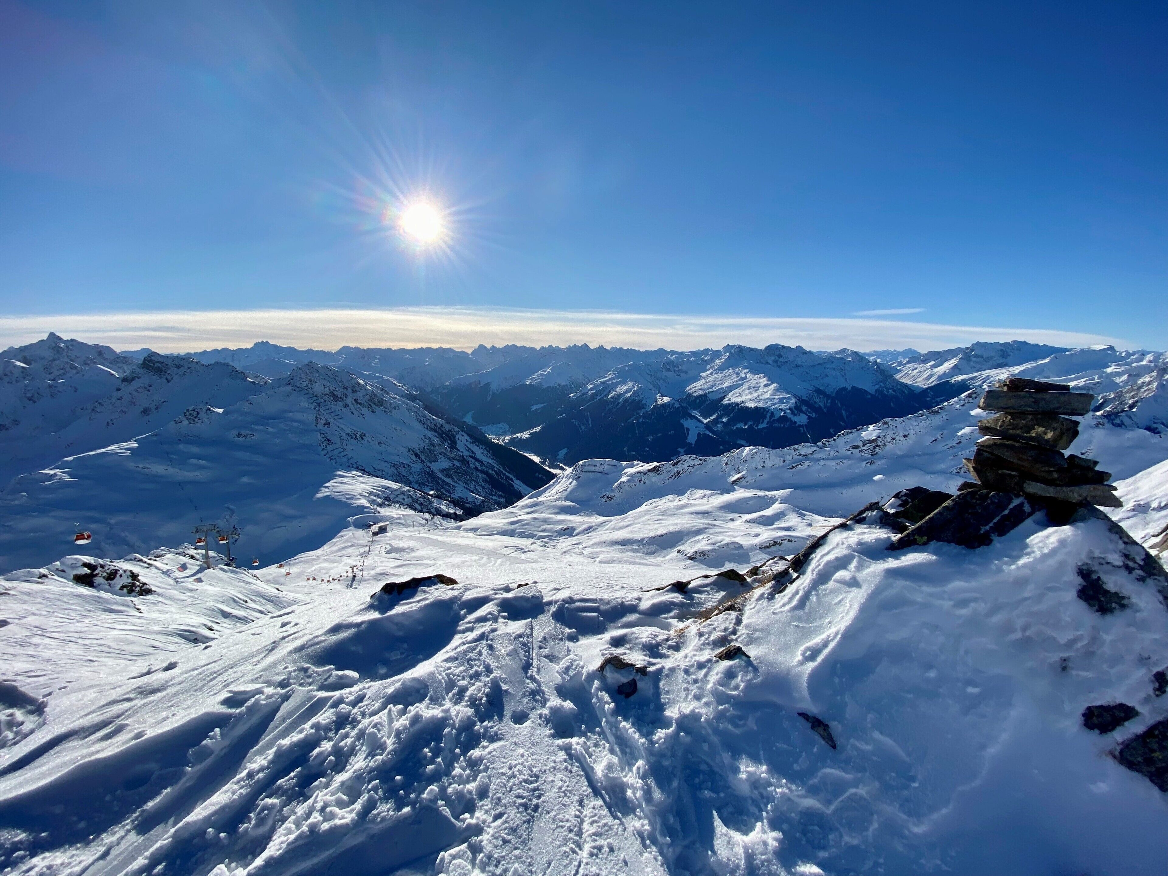 Paisagem montanhosa coberta de neve, com céu limpo e sol brilhando.