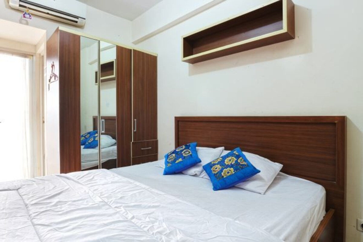 Um quarto com cama, guarda-roupa, espelho e prateleira.