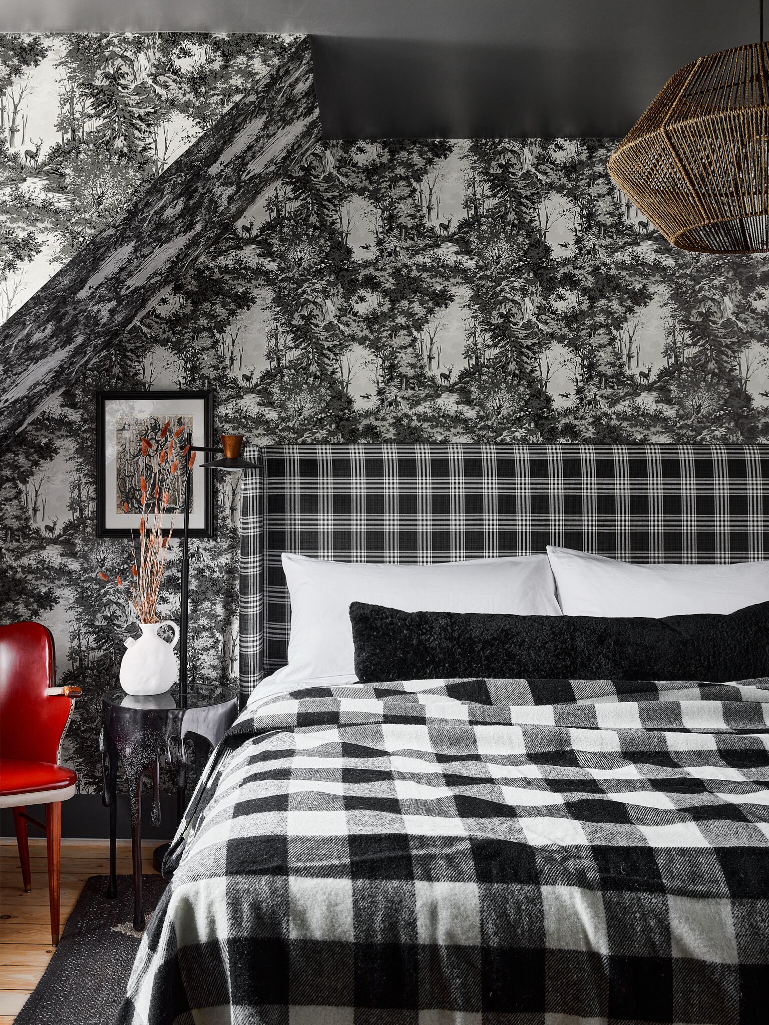 Quarto com colcha xadrez, cabeceira riscada e papel de parede com tema de floresta.