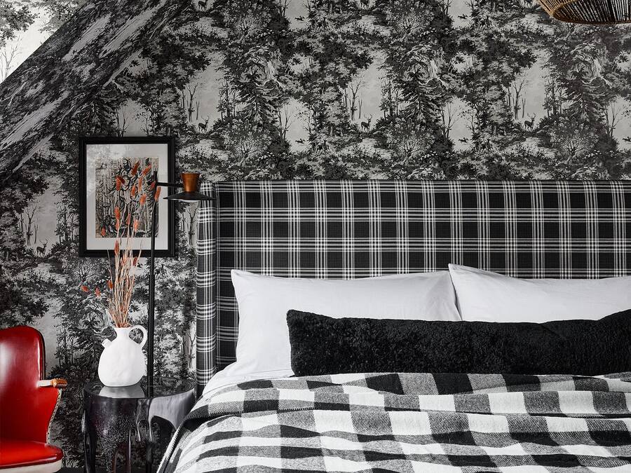 Quarto com colcha xadrez, cabeceira riscada e papel de parede com tema de floresta.