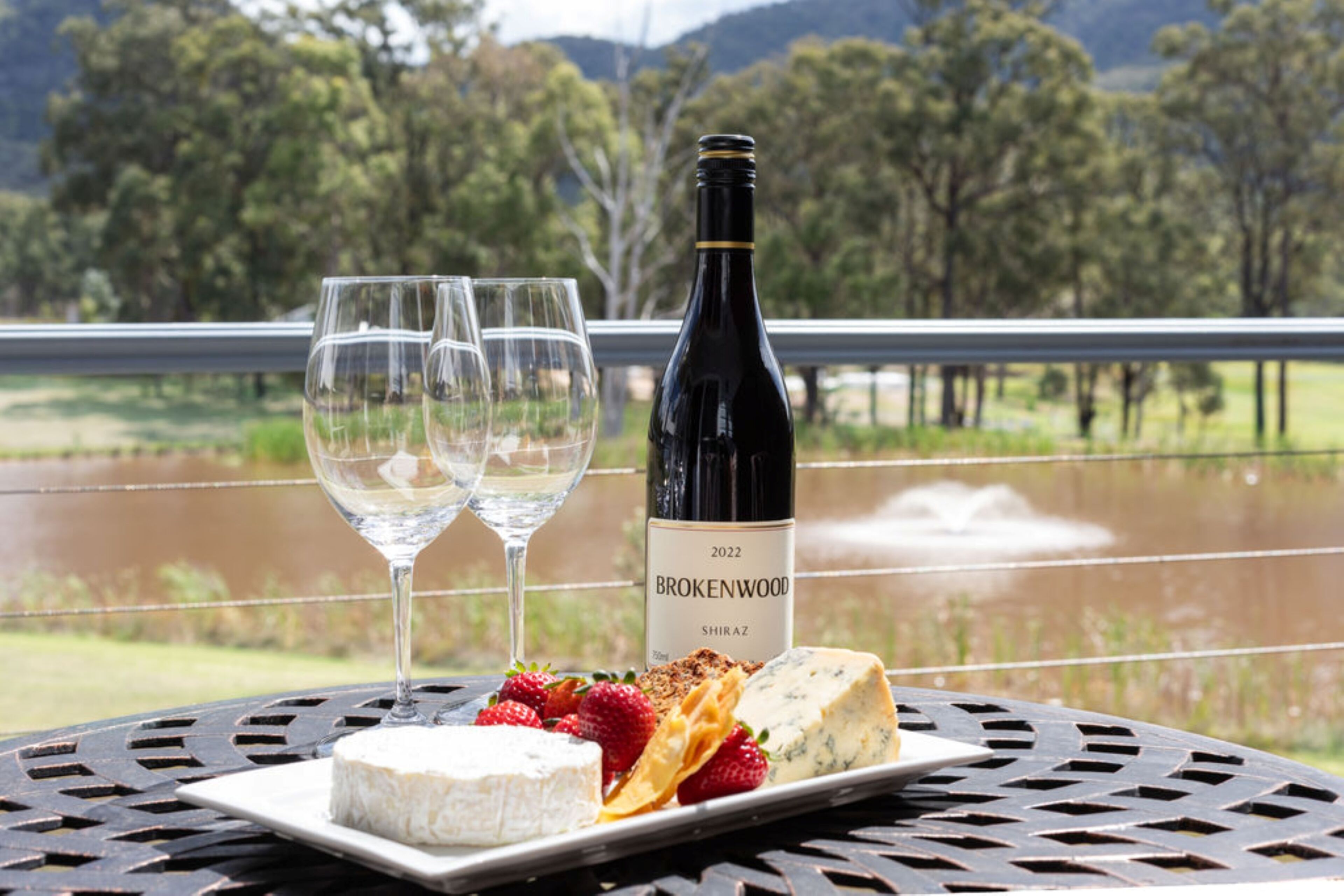 Uma mesa com uma garrafa de vinho, duas taças e um prato de queijo e morangos.
