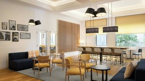 Um hall de hotel moderno com sofá, cadeiras, área de refeições, obras de arte nas paredes e iluminação pendente.