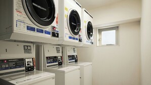 Uma lavanderia com várias máquinas de lavar e secar, uma janela e um painel de controle.