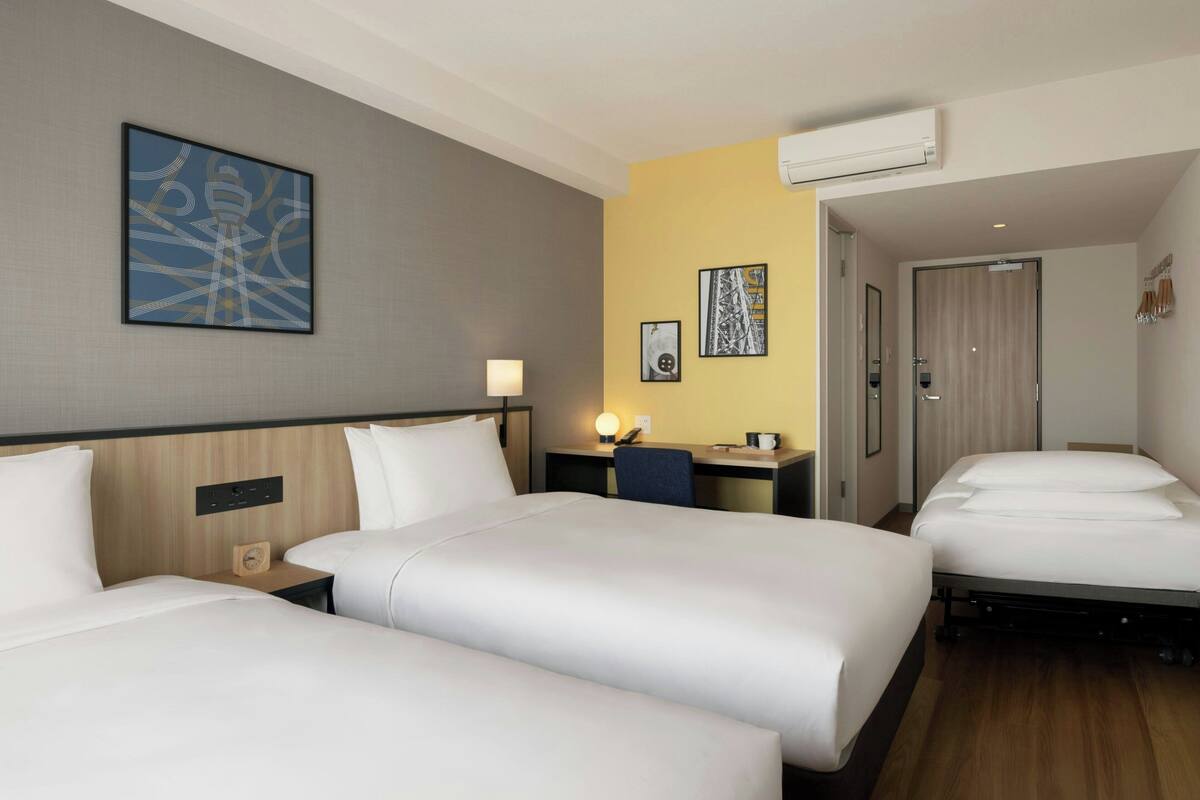 Quarto de hotel com duas camas, uma secretária com abajur e obras de arte nas paredes.