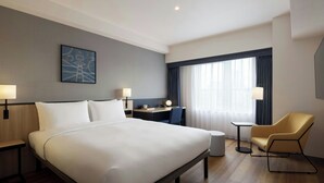 Quarto de hotel com uma cama grande, uma escrivaninha, uma cadeira e uma televisão.