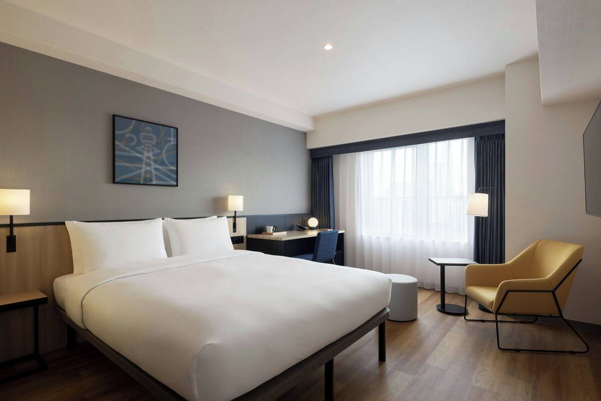 Quarto de hotel com uma cama grande, uma escrivaninha, uma cadeira e uma televisão.