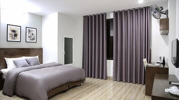 Quarto de hotel moderno com uma cama grande, uma escrivaninha, uma cadeira e uma janela com cortinas.