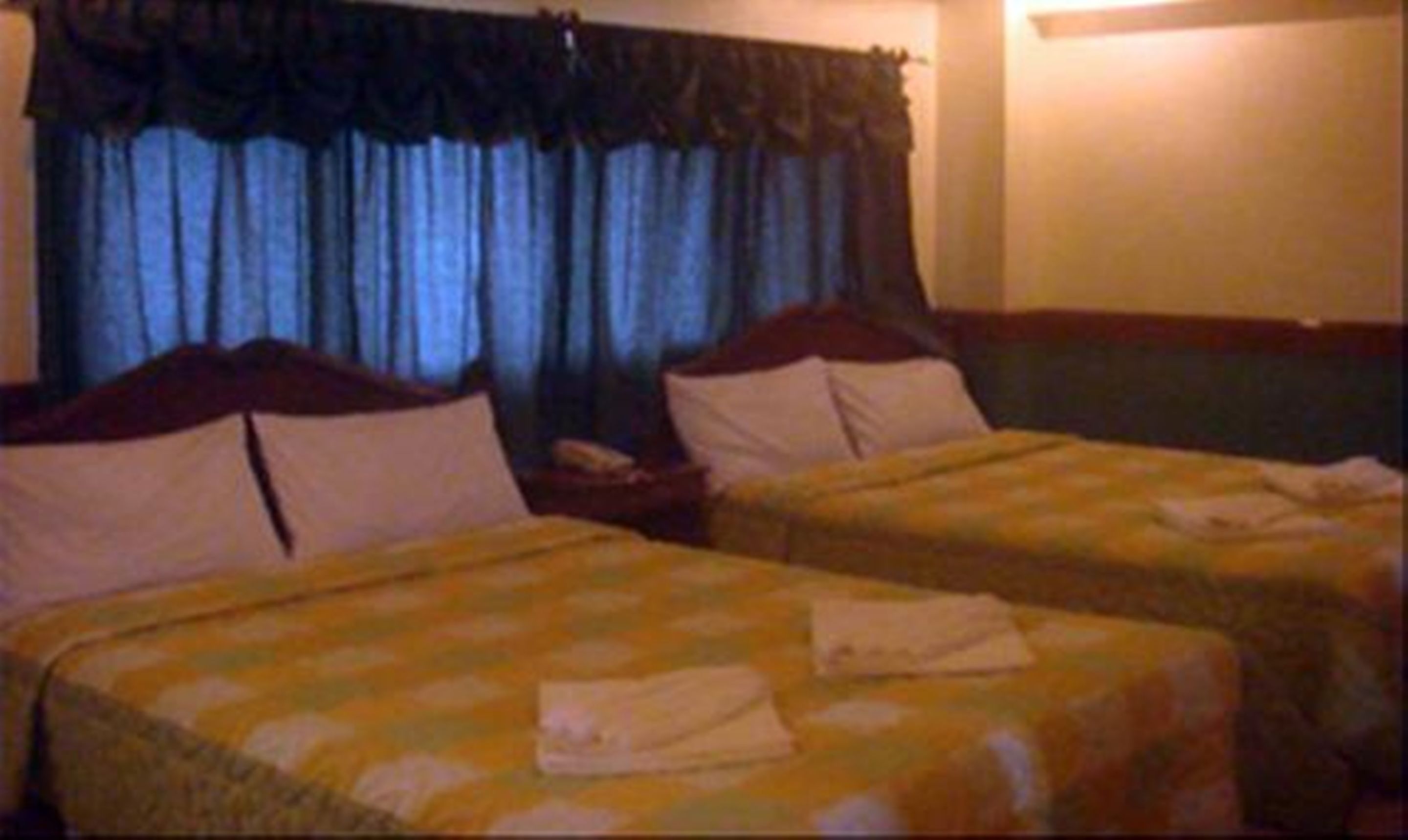 Quarto de hotel com duas camas, cada uma com colcha quadriculada amarela e branca, almofadas brancas e cortina azul escura.