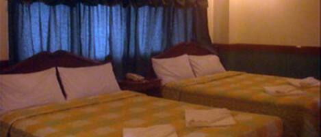 Quarto de hotel com duas camas, cada uma com colcha quadriculada amarela e branca, almofadas brancas e cortina azul escura.