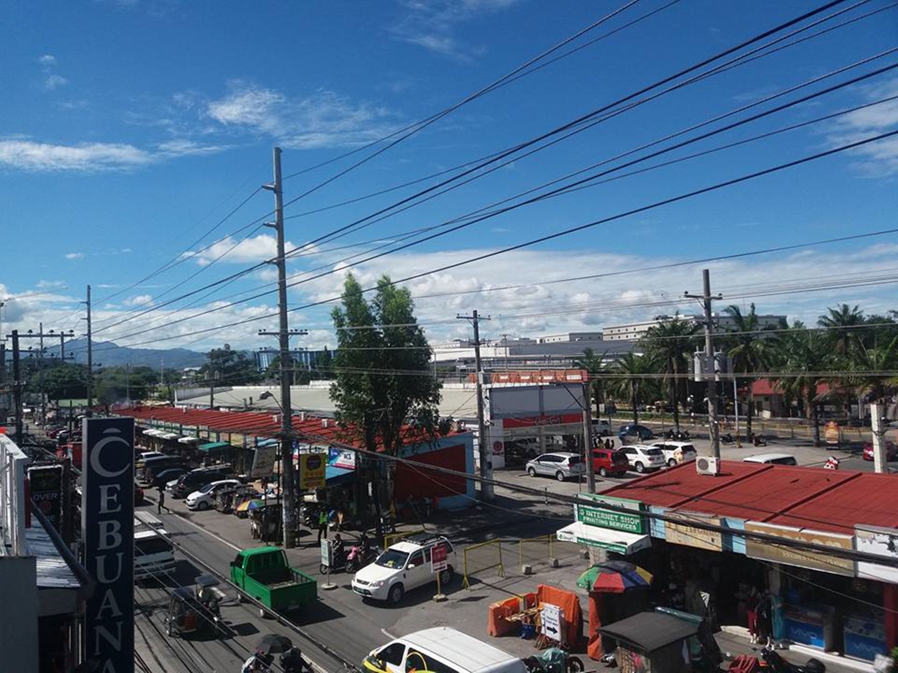 Ruas movimentadas da cidade com vários veículos, lojas e linhas de energia.