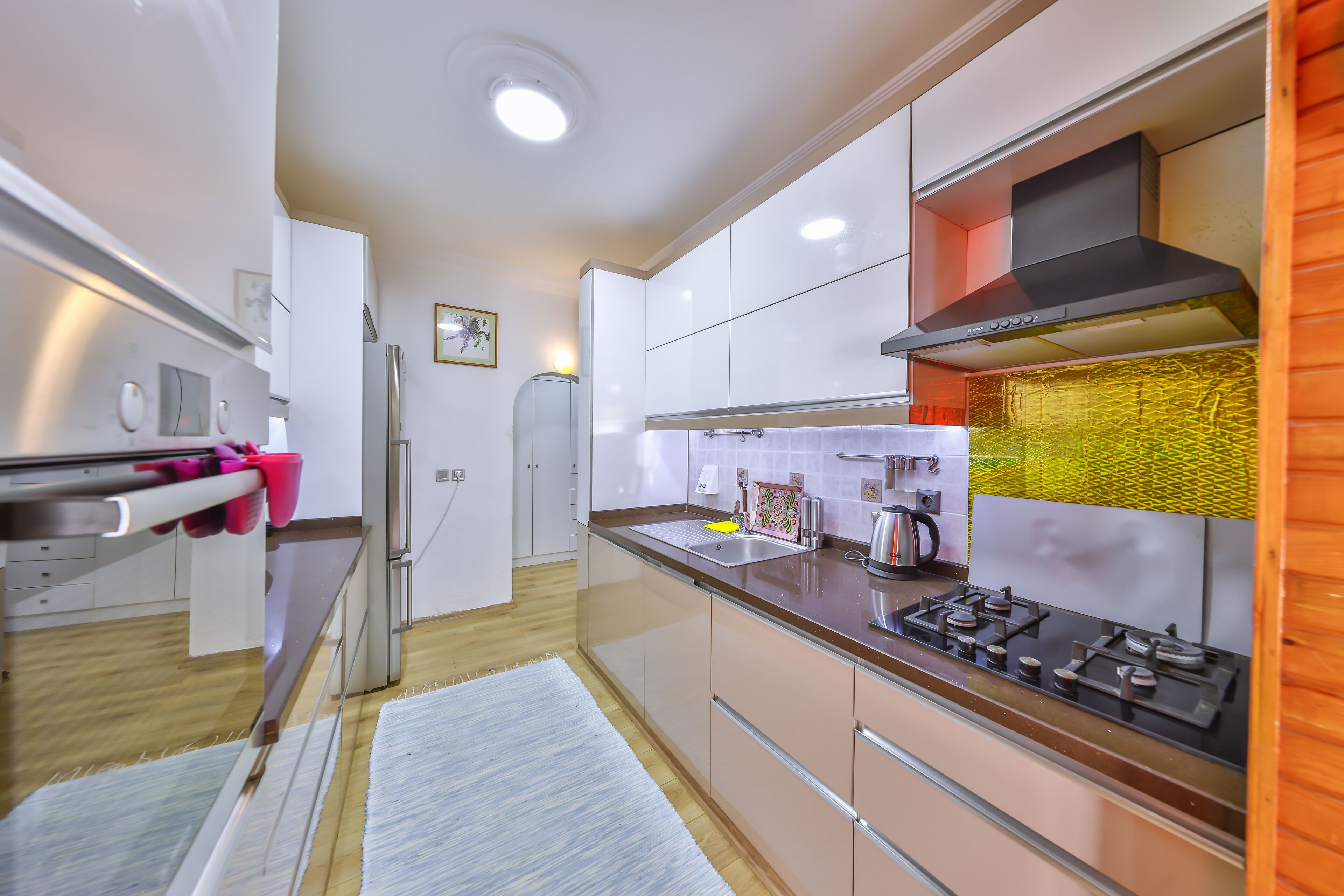 Uma cozinha moderna com armários brancos, coifa de aço inoxidável e backsplash amarela estampada.