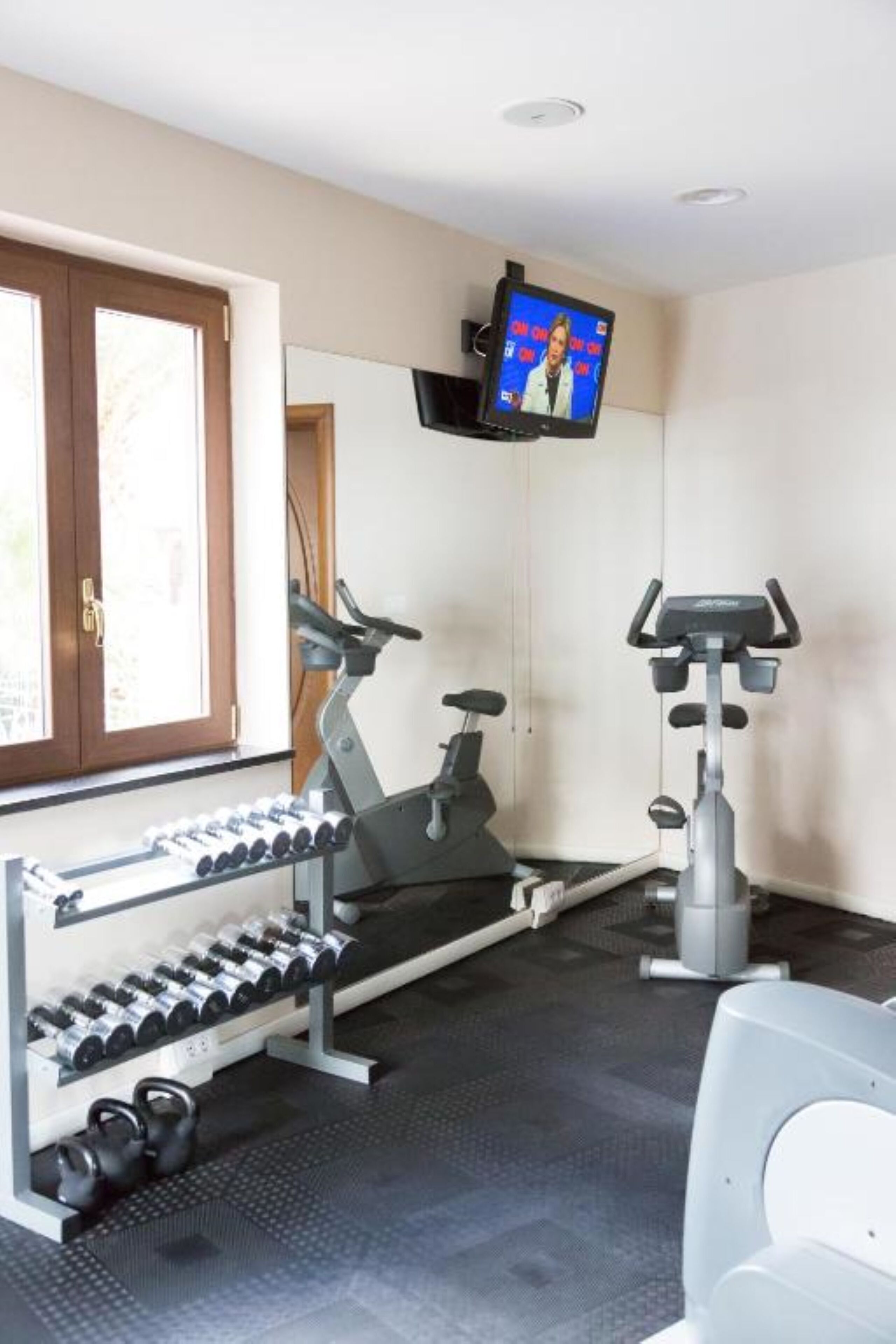 Uma academia com equipamentos de ginástica, uma televisão e uma janela com persianas.