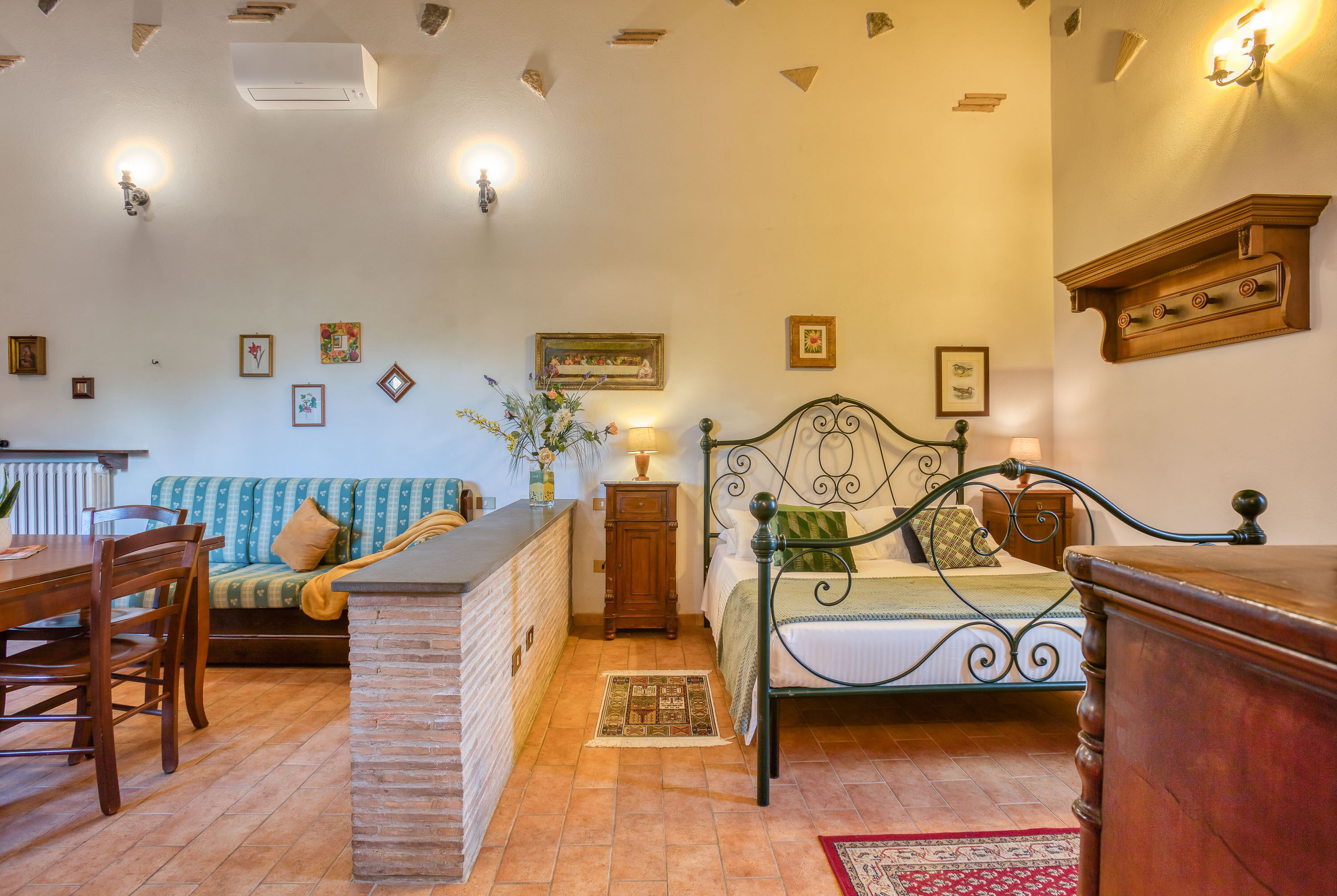 Quarto com cama, cômoda de madeira, mesa de jantar com cadeiras, lareira de tijolos e prateleira fixada na parede.