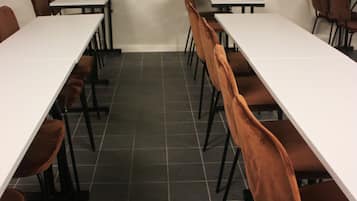 Uma sala de conferências com mesas compridas e cadeiras, cartazes nas paredes e piso de azulejos.