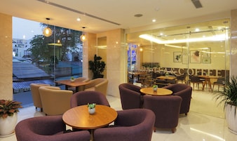 Interior moderno de café com mesas redondas e cadeiras estofadas, grandes janelas com vista para a paisagem urbana, e uma parede de vidro com o nome 'DATEA & COFFEE'.