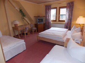 Quarto de hotel com duas camas de solteiro, uma mesa com cadeira, televisão e janela com cortinas.