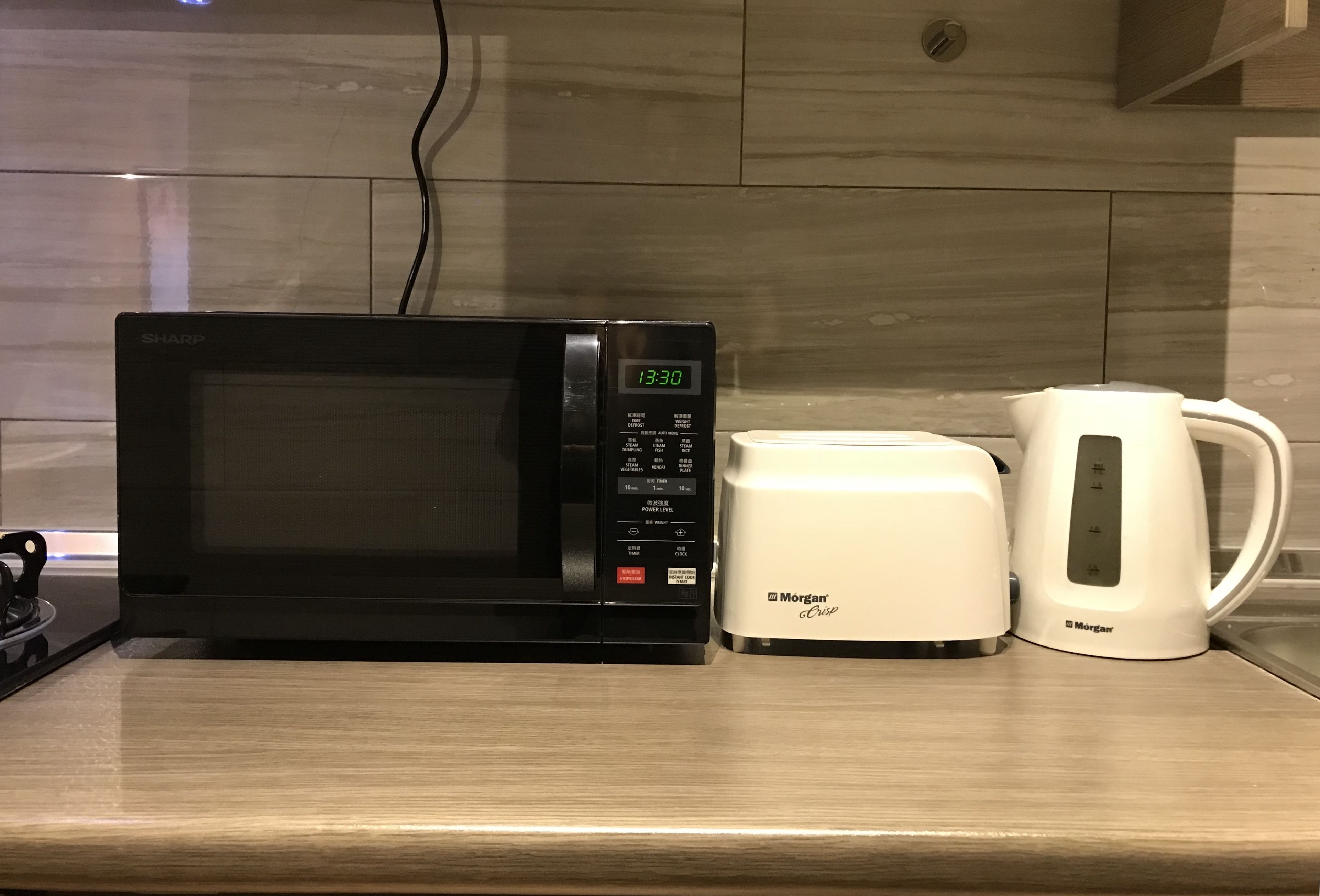 Um micro-ondas, uma cafeteira branca e uma chaleira elétrica branca em uma bancada de cozinha.