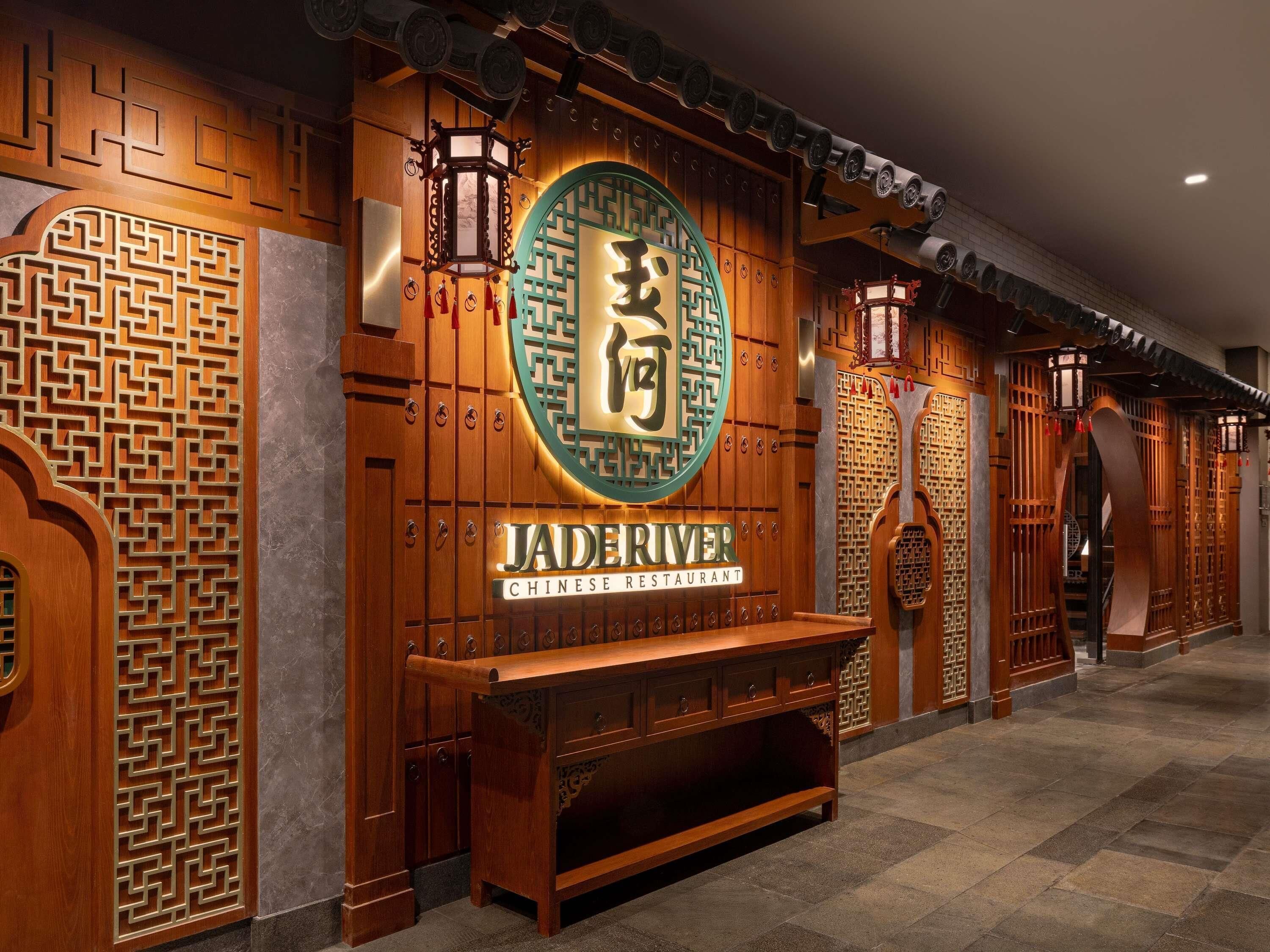 Interior de um restaurante tradicional chinês, com painéis de madeira, uma placa com a inscrição 'Jade River Chinese Restaurant' e um banco ao centro.