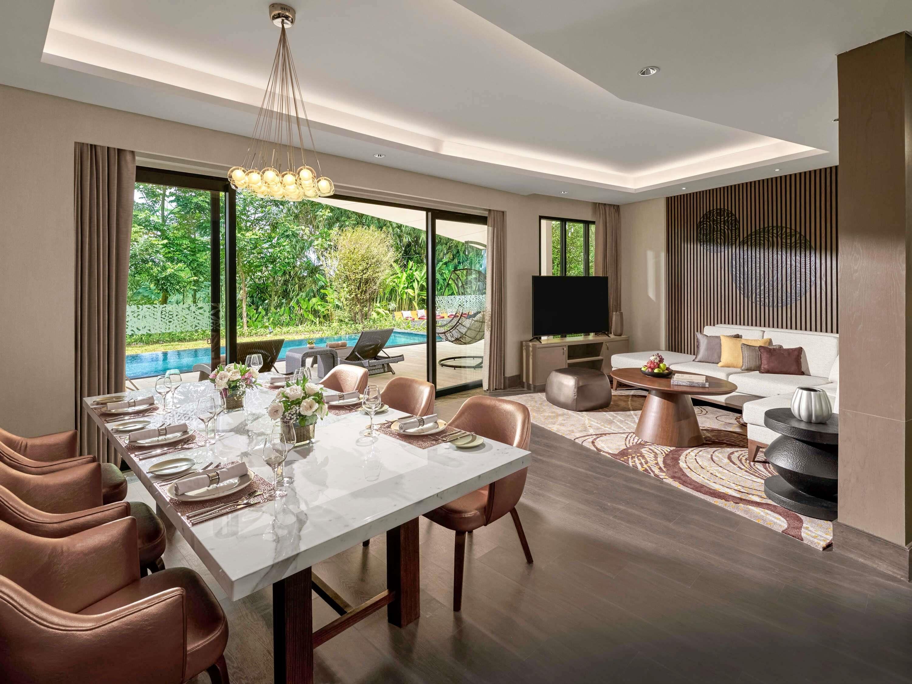 Uma sala de jantar moderna com uma mesa grande posta para seis, um sofá e uma TV em uma área de estar com vista para a piscina.
