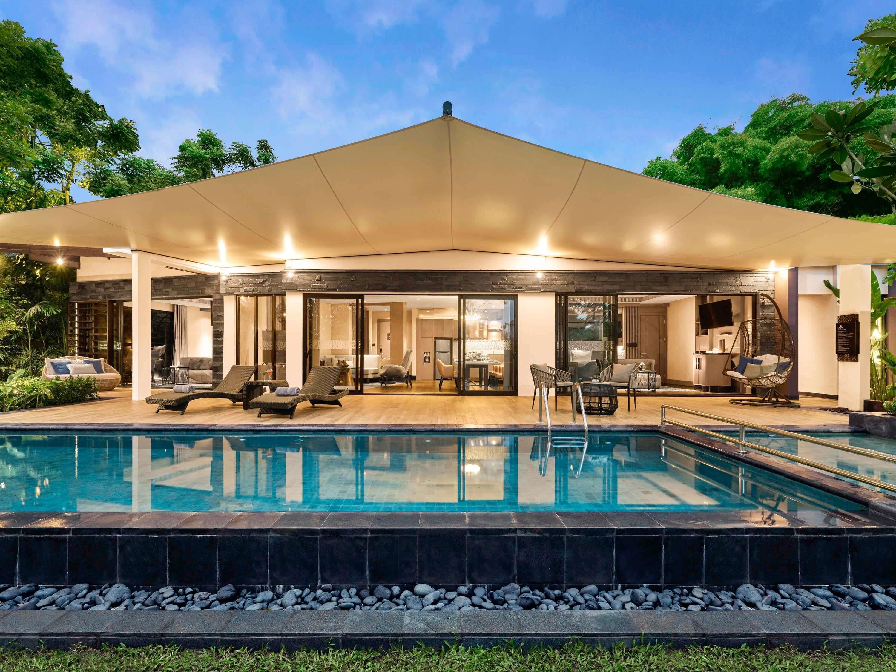 Área à beira da piscina com espreguiçadeiras, um espaço de estar coberto e vista para a piscina.