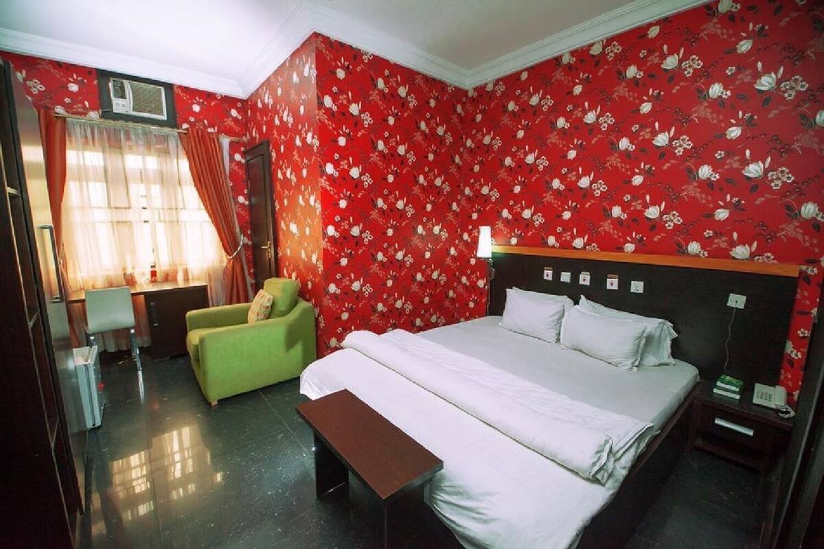 Quarto de hotel com uma cama, uma mesa, uma cadeira e uma janela com cortinas.