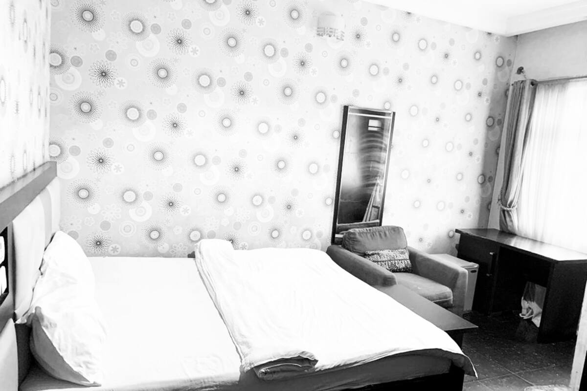 Quarto de hotel com cama, escrivaninha, cadeira, espelho e papel de parede estampado.