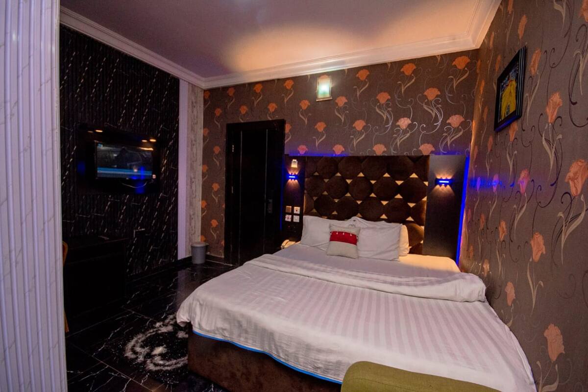 Quarto de hotel com uma cama grande, televisão, aquecedor fixado na parede e papel de parede estampado.