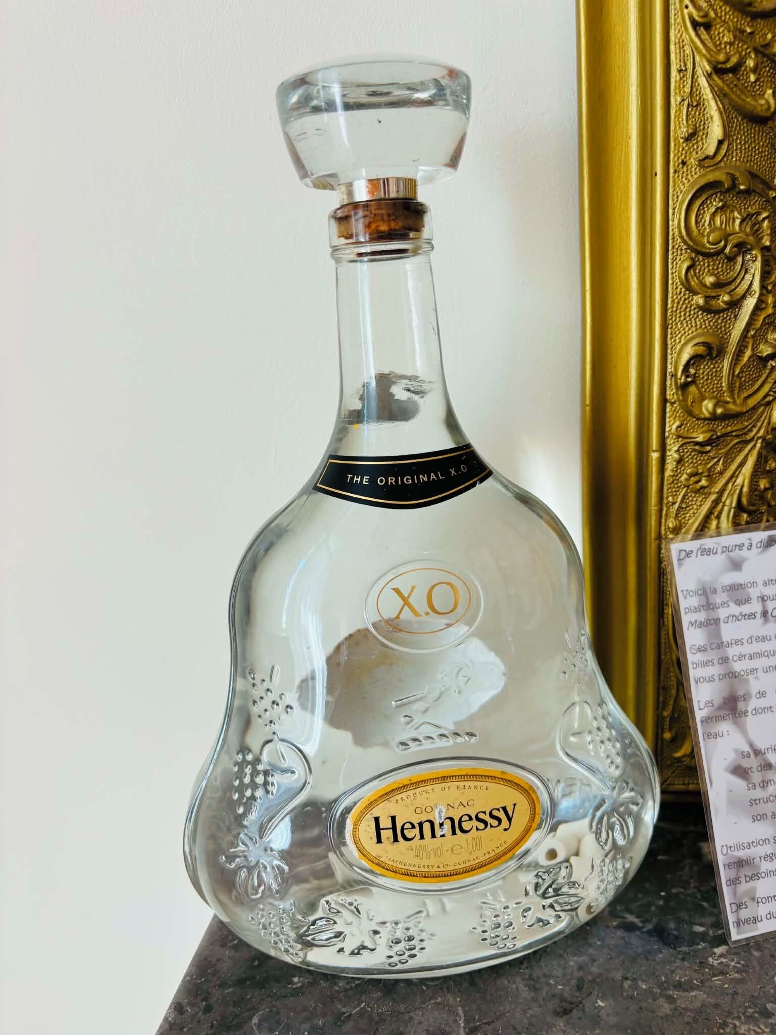 Uma garrafa de vidro transparente com uma etiqueta que diz 'Hennessy' e 'X.O' sobre uma superfície de mármore.