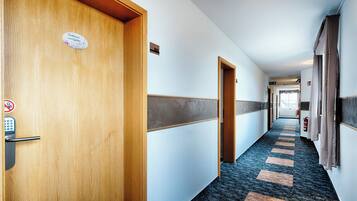 Um corredor de hotel com porta de madeira, fechadura eletrônica, placa com nome e tapete azul estampado.