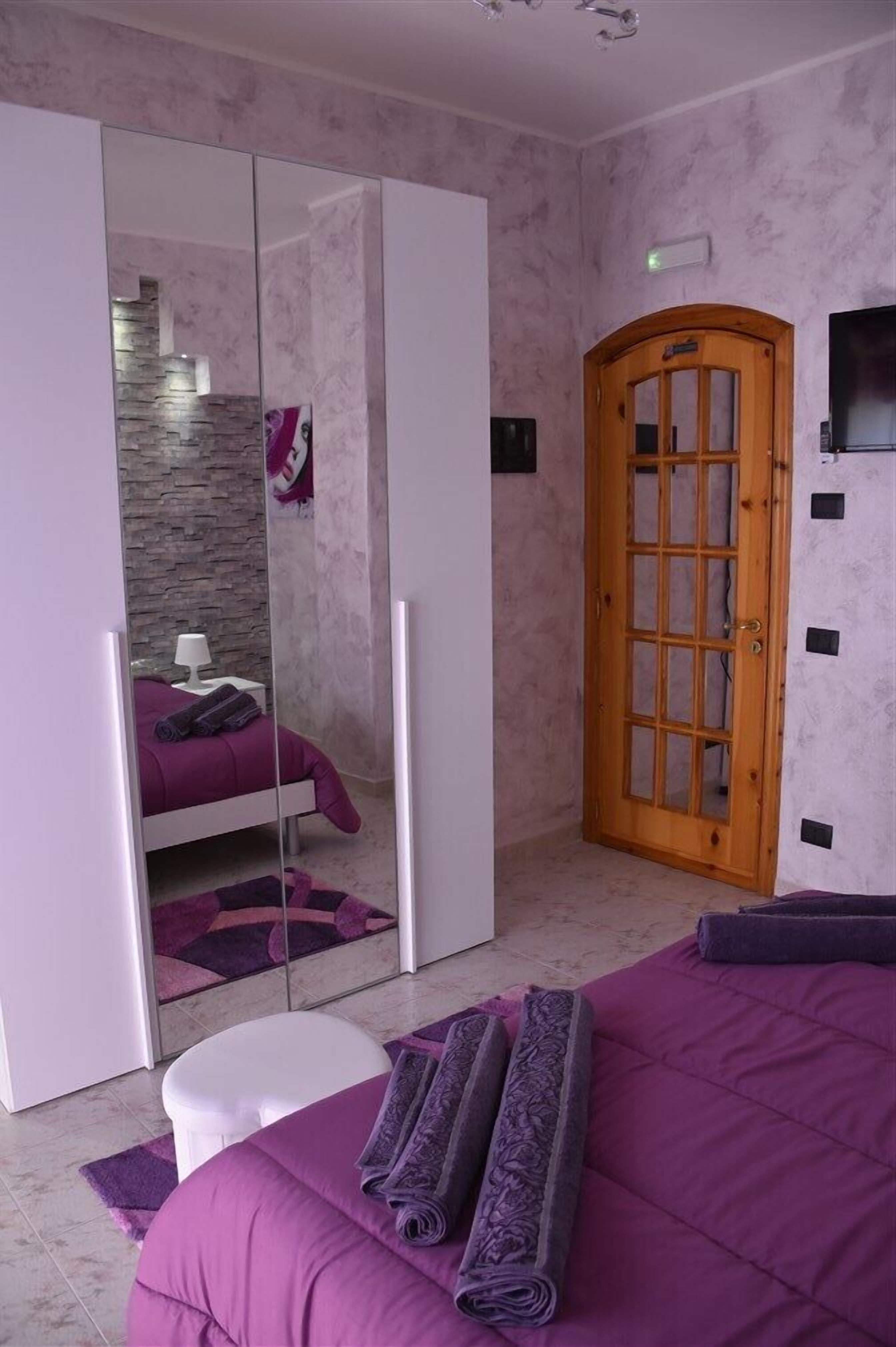 Quarto com cama, guarda-roupa, porta e televisão fixada na parede.