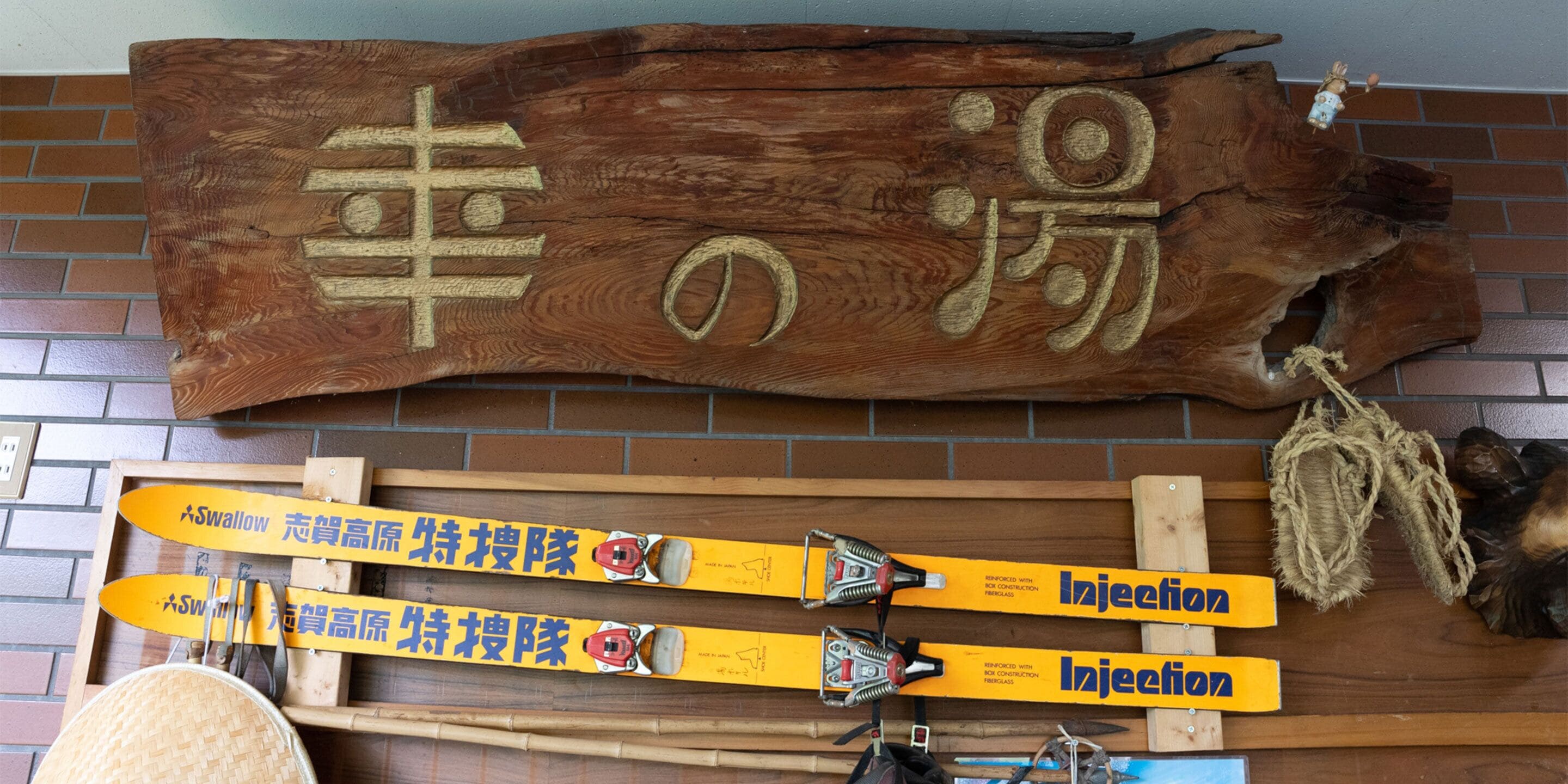 Uma placa de madeira com caracteres japoneses e dois esquis amarelos com a marca 'Injection'.