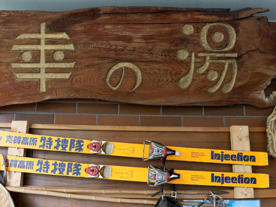 Uma placa de madeira com caracteres japoneses e dois esquis amarelos com a marca 'Injection'.