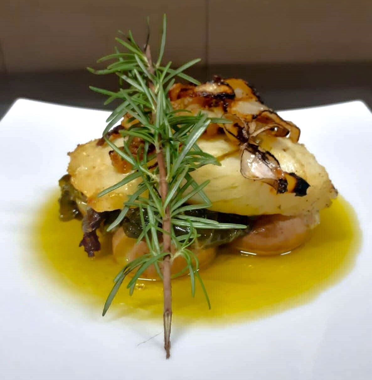 Prato com frango assado, legumes e um ramo de alecrim, servido em prato branco com um fio de azeite.