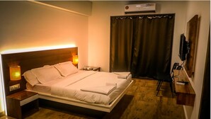 Quarto de hotel com cama, luminárias de cabeceira, escrivaninha com cadeira, televisão e ar condicionado.