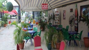Um café ao ar livre com mesas, cadeiras, plantas em vasos e um aviso indicando a possibilidade de pagamento eletrônico.