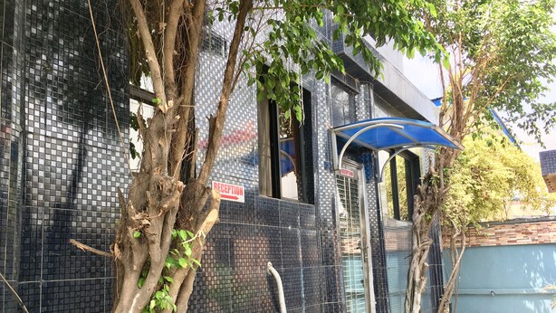 Um edifício com área de recepção, fachada em azulejos e uma árvore em primeiro plano.