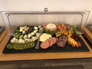 Uma tábua de frios com diversos queijos, carnes, frutas e legumes.