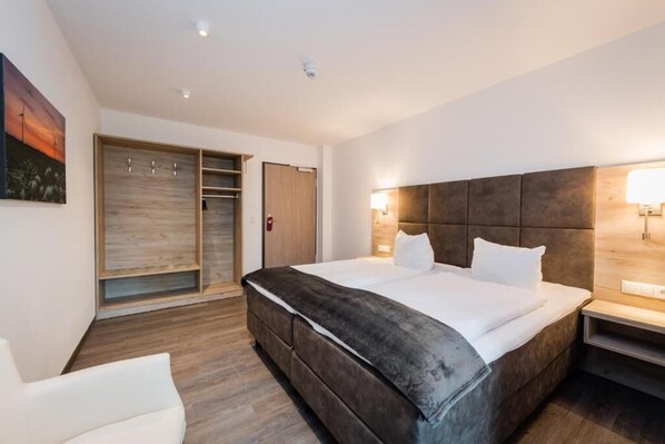 Quarto de hotel moderno com uma cama grande, um guarda-roupa e uma mesinha de cabeceira.