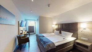 Quarto de hotel moderno com uma cama grande, mesas de cabeceira, uma escrivaninha com cadeira e uma televisão.