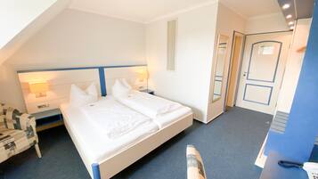 Quarto de hotel com uma cama grande, uma mesa e uma cadeira. Há um espelho na parede e uma porta com moldura azul.